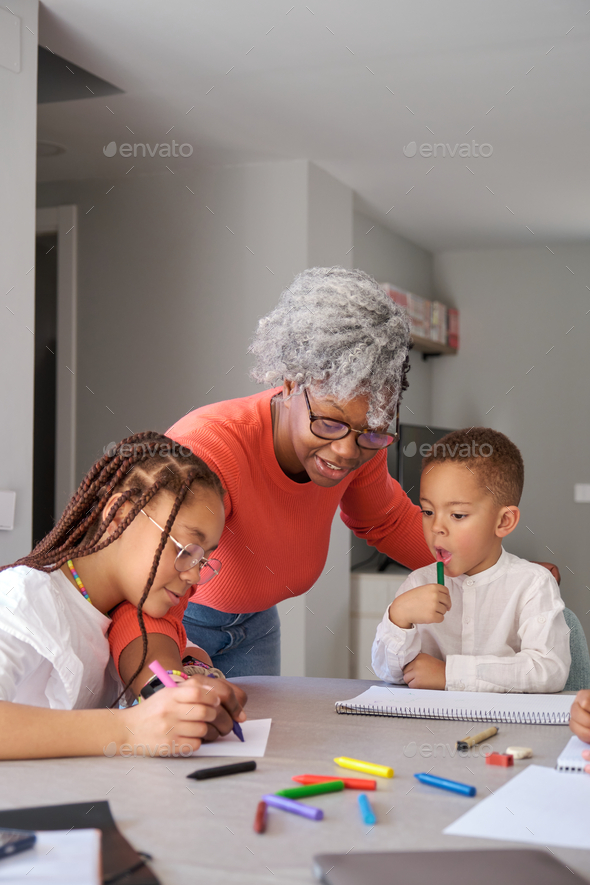 African mother helping her daughter with homework while her son is painting. Stock Photo by ...